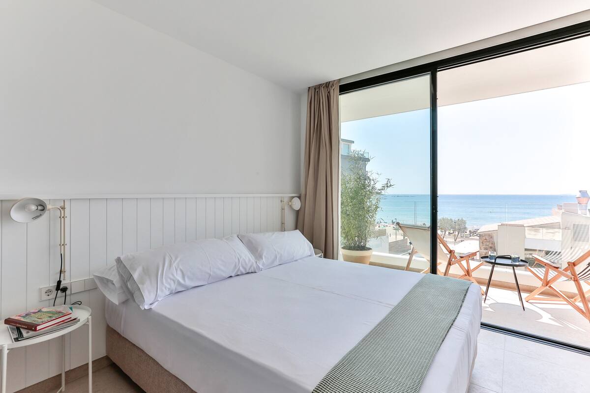 Quarto de hotel com uma cama, mesa de cabeceira, abajur e vista para o mar.