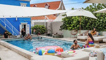 Uma área de piscina com espreguiçadeiras, um boi de água colorido e uma escada que leva a uma porta.