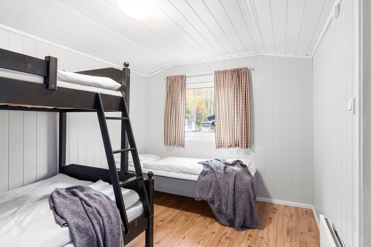 Quarto com beliche, escada, janela com cortinas e radiador.