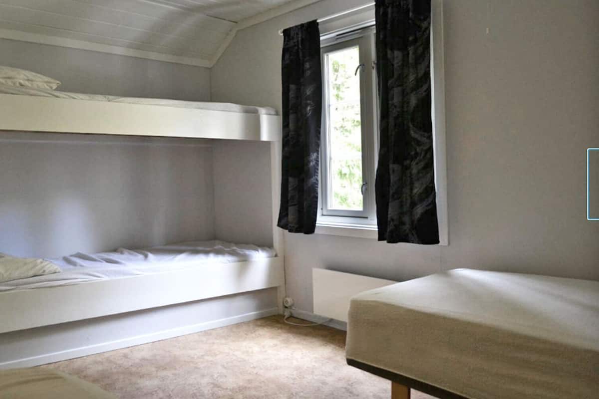 Um quarto com beliches, uma janela com cortinas e um radiador.