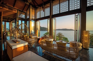 Quarto espaçoso com uma grande janela com vista para a água, mobiliado com móveis de vime e uma mesa de centro de vidro.