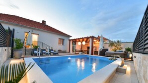 Uma piscina com um terraço coberto, uma parede de pedra e uma casa com telhado em cerâmica.