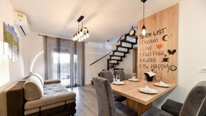 Uma sala de estar moderna com sofá, mesa de jantar e cadeiras. Há uma escada que leva a outro andar.