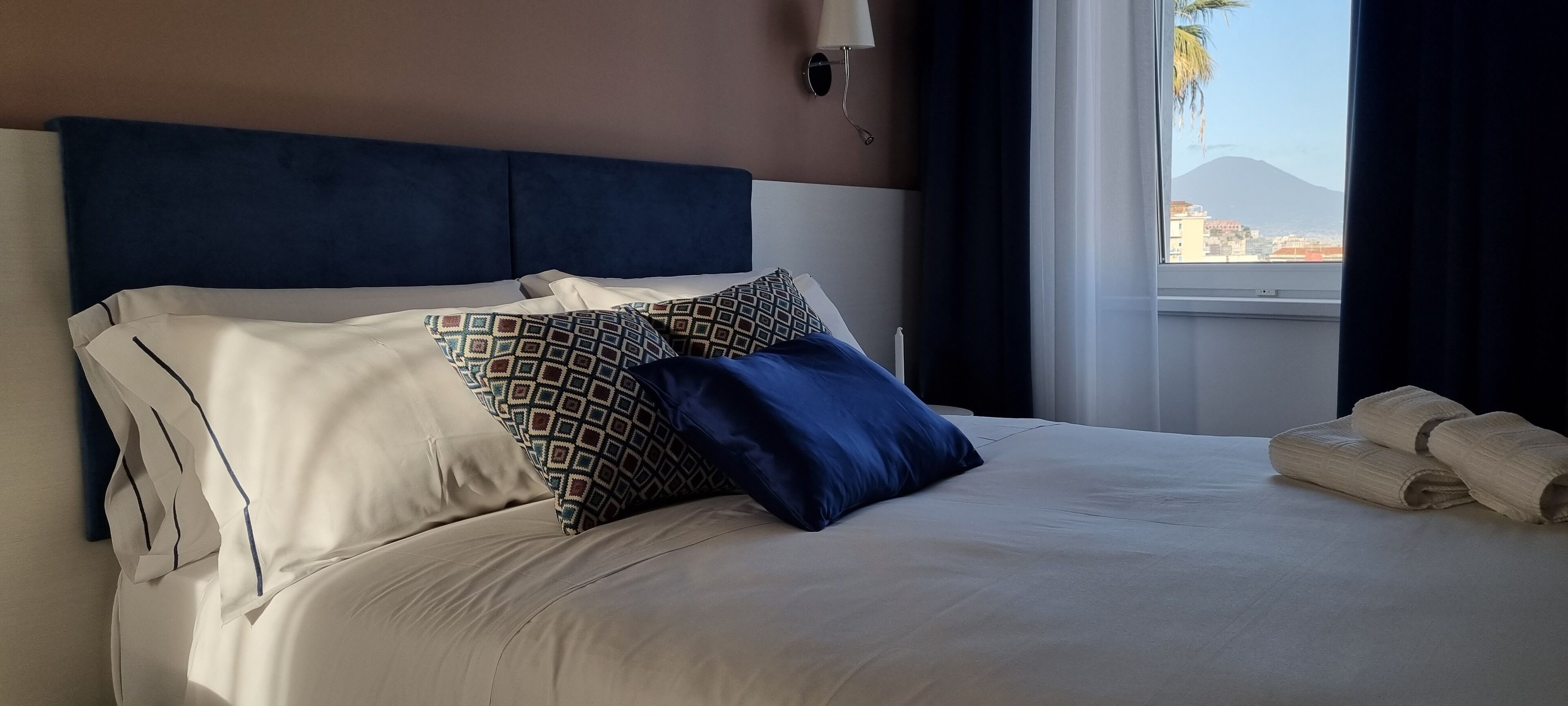 Cama bem arrumada com almofadas estampadas, cabeceira e janela com vista para a montanha.