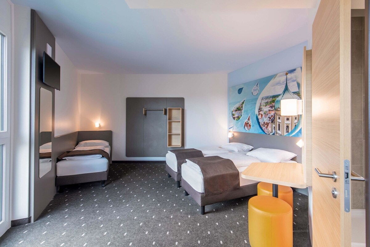 Quarto de hotel com duas camas, um espelho grande, um quadro e uma mesinha de cabeceira com abajur.