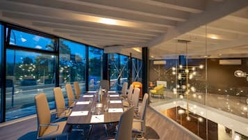Uma sala de conferências moderna com uma mesa comprida, várias cadeiras e grandes janelas com vista para o exterior.