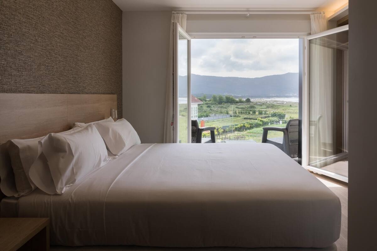 Quarto de hotel com uma cama grande, vista para um vinhedo e varanda com uma cadeira.