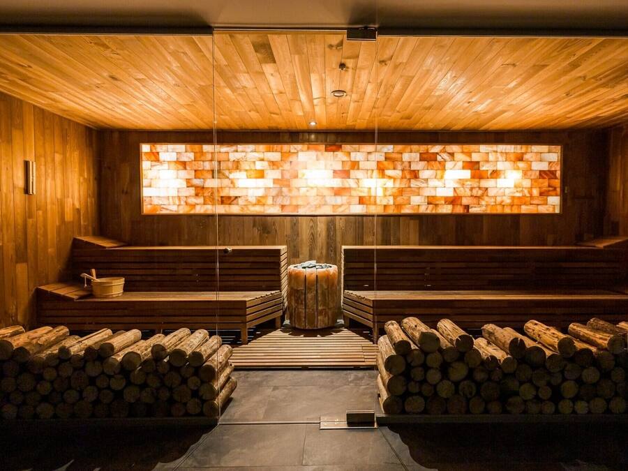Uma sauna com bancos de madeira, um banco central aquecido de pedra e lenha empilhada em ambos os lados.