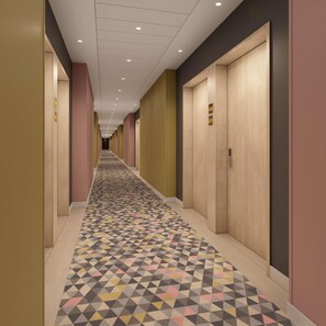 Um corredor de hotel com carpete estampado, portas de madeira e teto com iluminação embutida.