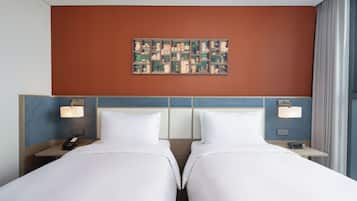 Quarto de hotel com duas camas, cabeceira com prateleira embutida, abajures e uma obra de arte pendurada na parede.