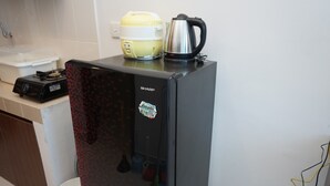 Uma cozinha compacta com geladeira preta, fogão a gás, chaleira e pia pequena.