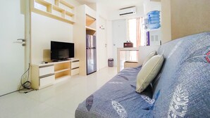 Um espaço de estar compacto com sofá, televisão, frigorífico e dispensador de água.