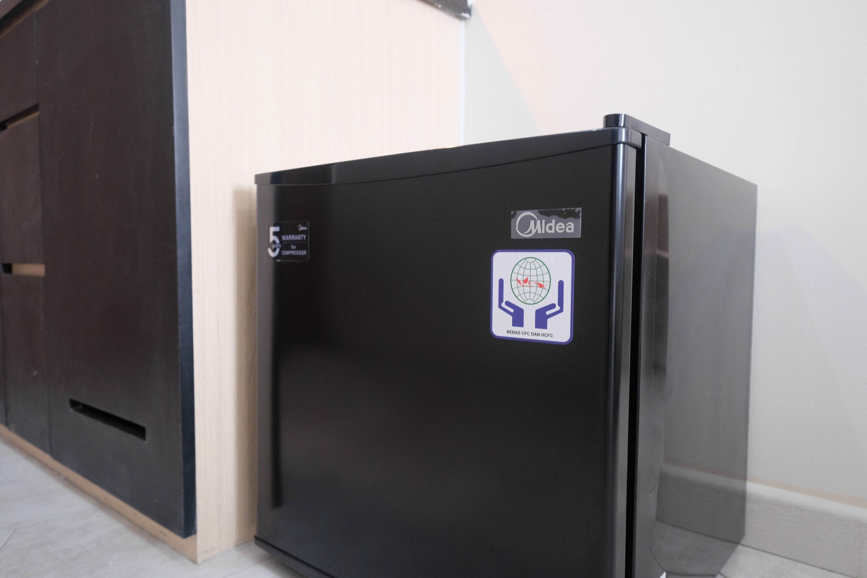 Uma geladeira preta com adesivo indicando garantia de 5 anos e o logotipo da Midea.