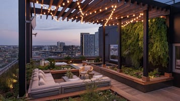 Terraço no telhado com pérgola de madeira, luzes de corda, área de estar acolchoada e jardim vertical.