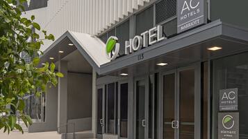 Uma entrada de hotel moderna com um sinal de AC Hotels Marriott em destaque, um logotipo verde e o número 115 na fachada.