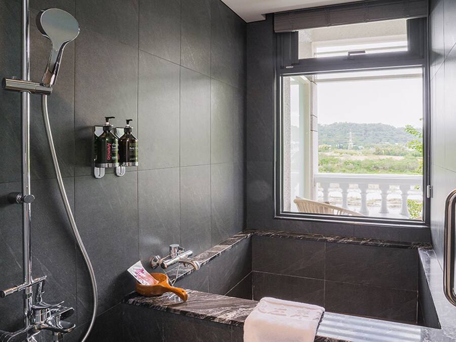 Uma casa de banho moderna com chuveiro, janela com vista e artigos de higiene no muro.