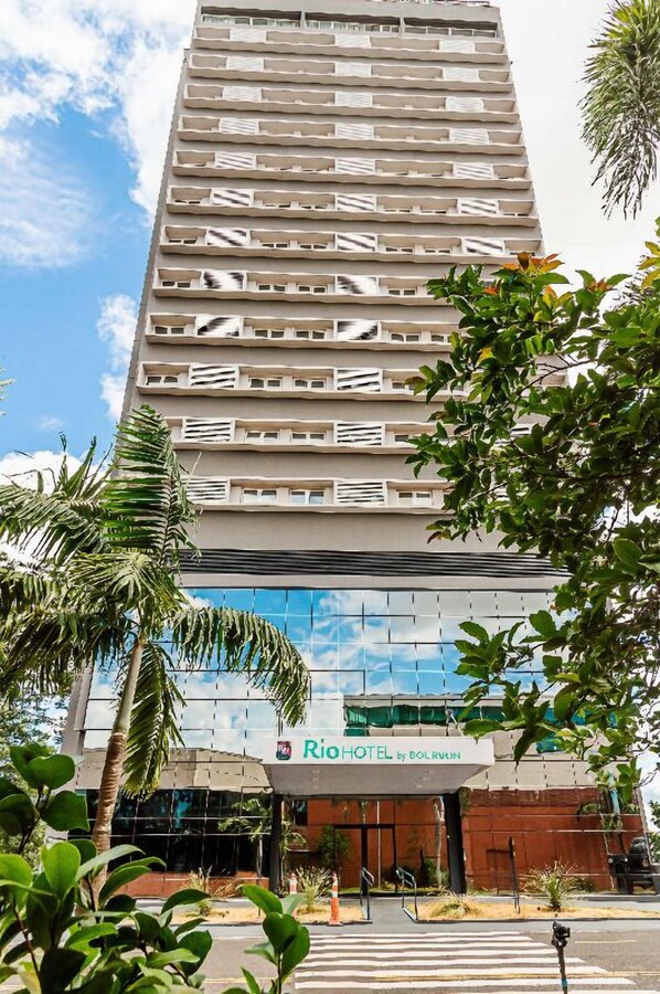 Um hotel alto com várias varandas, fachada de vidro e uma placa com a inscrição 'Rio Hotel by Bolivar'.