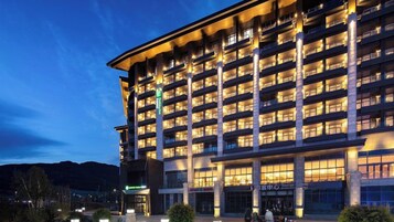 Um hotel de vários andares com design moderno, com varandas em cada pavimento e uma entrada imponente.