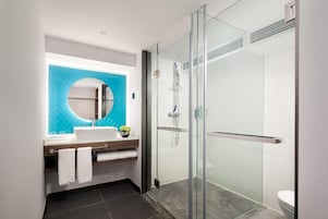 Uma casa de banho moderna com chuveiro em cabine de vidro, espelho redondo e lavatório branco.