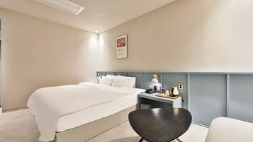 Quarto de hotel com cama, escrivaninha com luminária, cadeira e pequena mesa com telefone e luminária.