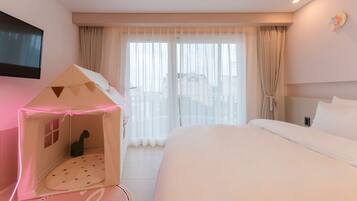 Quarto de hotel com cama, uma tenda de brincar, TV fixada na parede e janela com cortinas.
