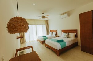 Quarto de hotel com duas camas, ventoinha no teto, aparelho de ar condicionado e um grande candeeiro de fibra natural.