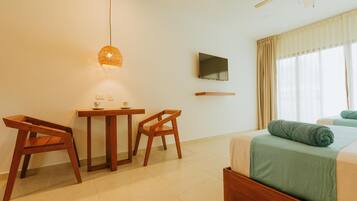 Quarto de hotel com cama, secretária e cadeiras, televisão na parede e janela com cortinas.