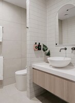Um banheiro moderno com uma pia branca, um espelho grande e um vaso sanitário.