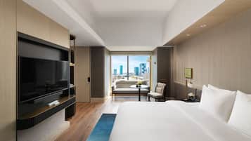 Quarto de hotel moderno com uma cama grande, televisão de tela plana, sofá e vista para a cidade.