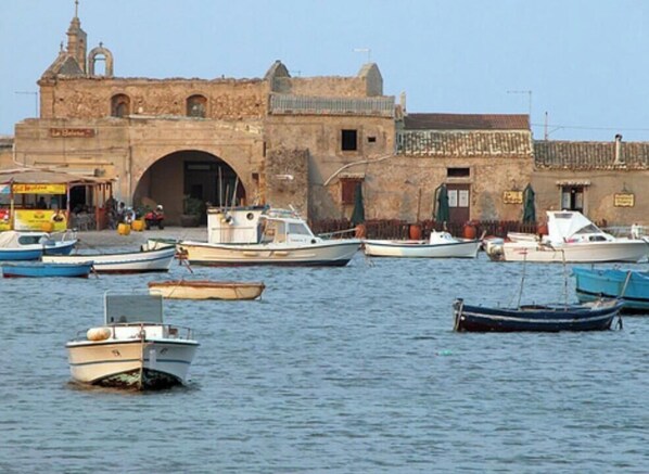 Um porto com vários barcos atracados e um edifício histórico com um grande arco ao fundo.