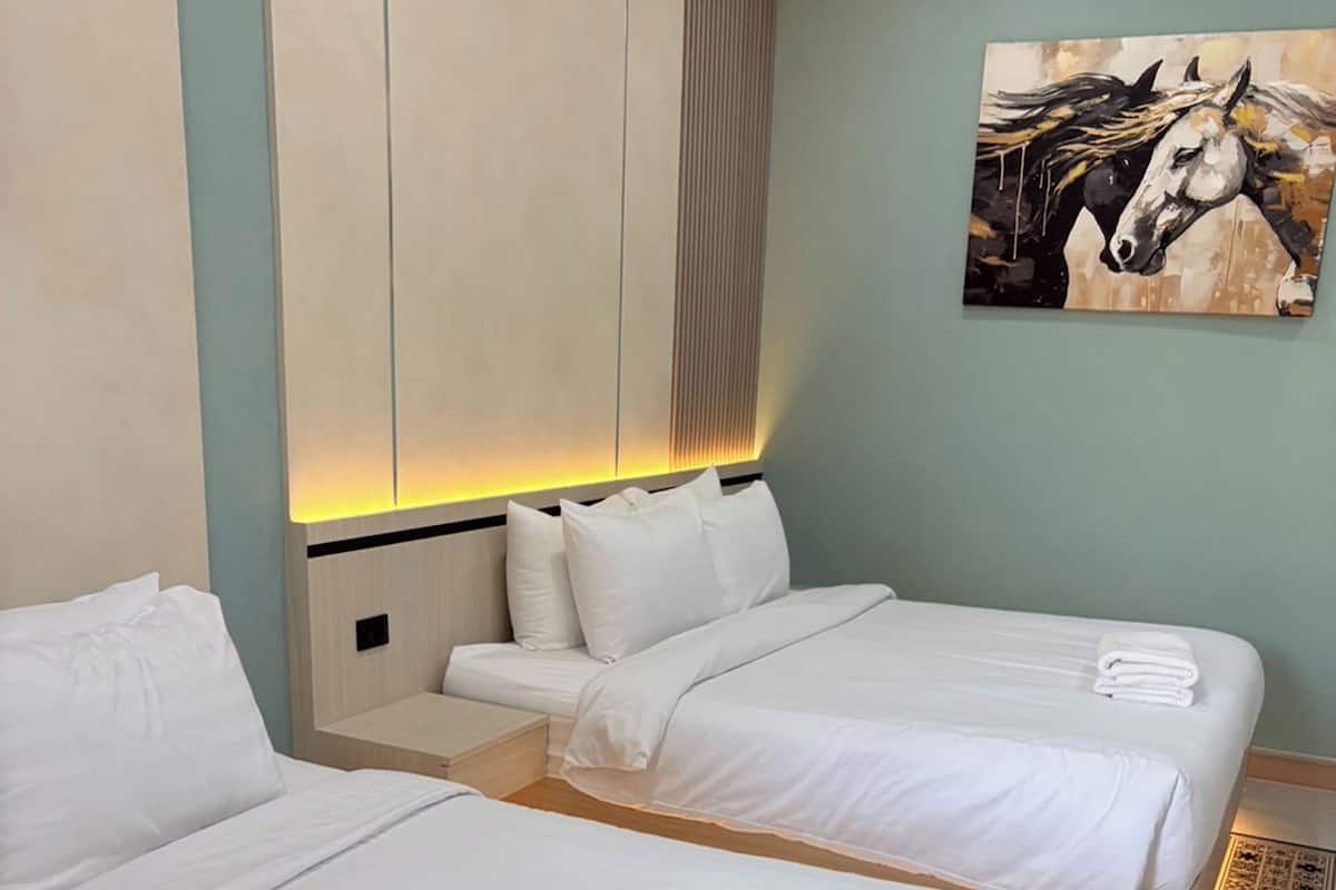 Quarto de hotel com duas camas, cabeceira, um quadro pendurado na parede e tapete estampado.
