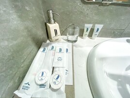 Um banheiro com pia branca, um frasco de loção, um copo d'água e vários tubos de creme.