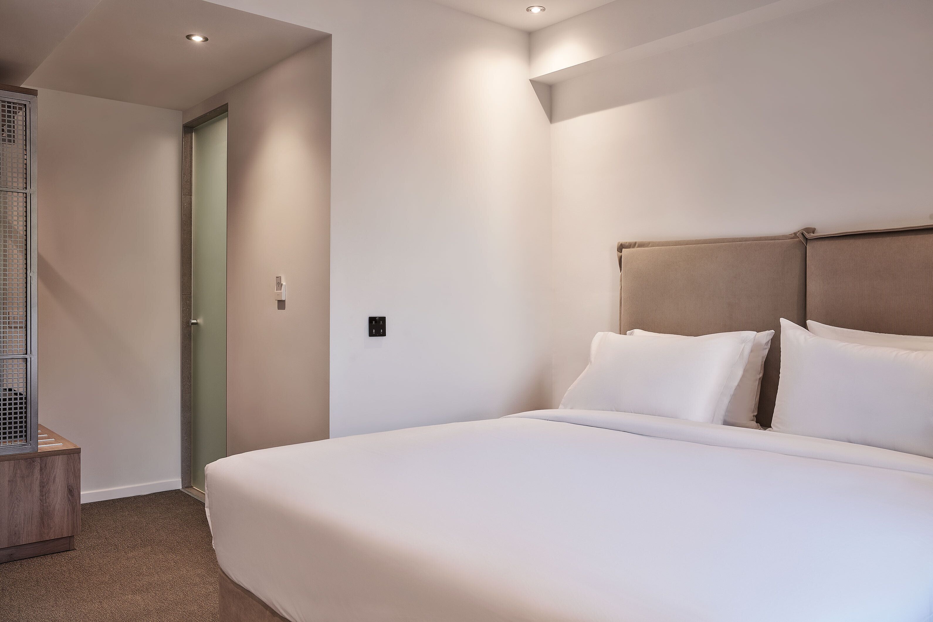 Quarto de hotel moderno com uma cama grande, uma cabeceira de madeira e uma pequena mesa de cabeceira.