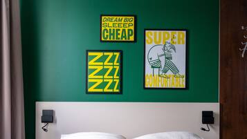 Quarto com parede verde, cama com roupa de cama branca e três cartazes motivacionais.