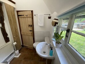 Casa de banho com porta de madeira, azulejos brancos, lavatório com espelho e uma planta em vaso.