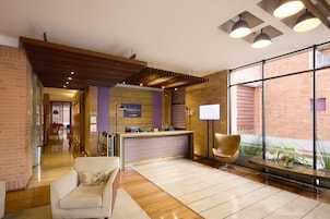 Uma área de recepção de hotel com balcão, uma sala de espera com sofá e uma janela ampla com vista para o exterior.
