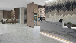 Um hall de hotel moderno com uma receção de mármore, zona de bar e espaço de estar.