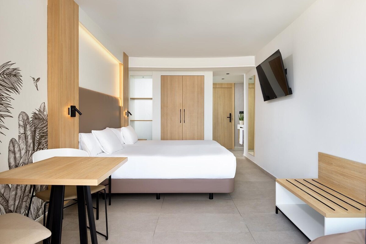 Quarto moderno com cama, mesa de cabeceira e escrivaninha com cadeiras.