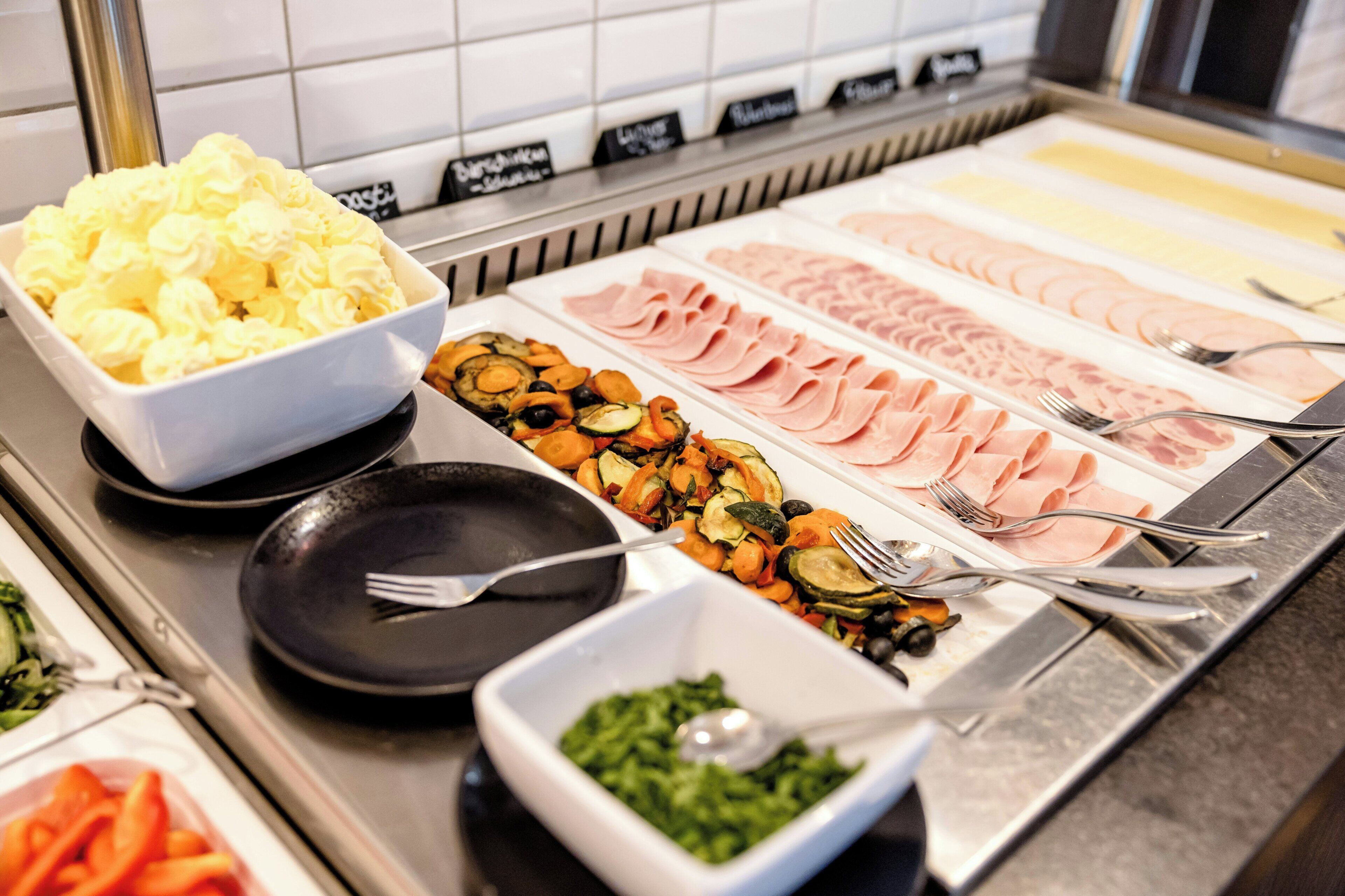 Buffet com diversas opções de comida, incluindo legumes, carnes e uma tigela de chantilly.
