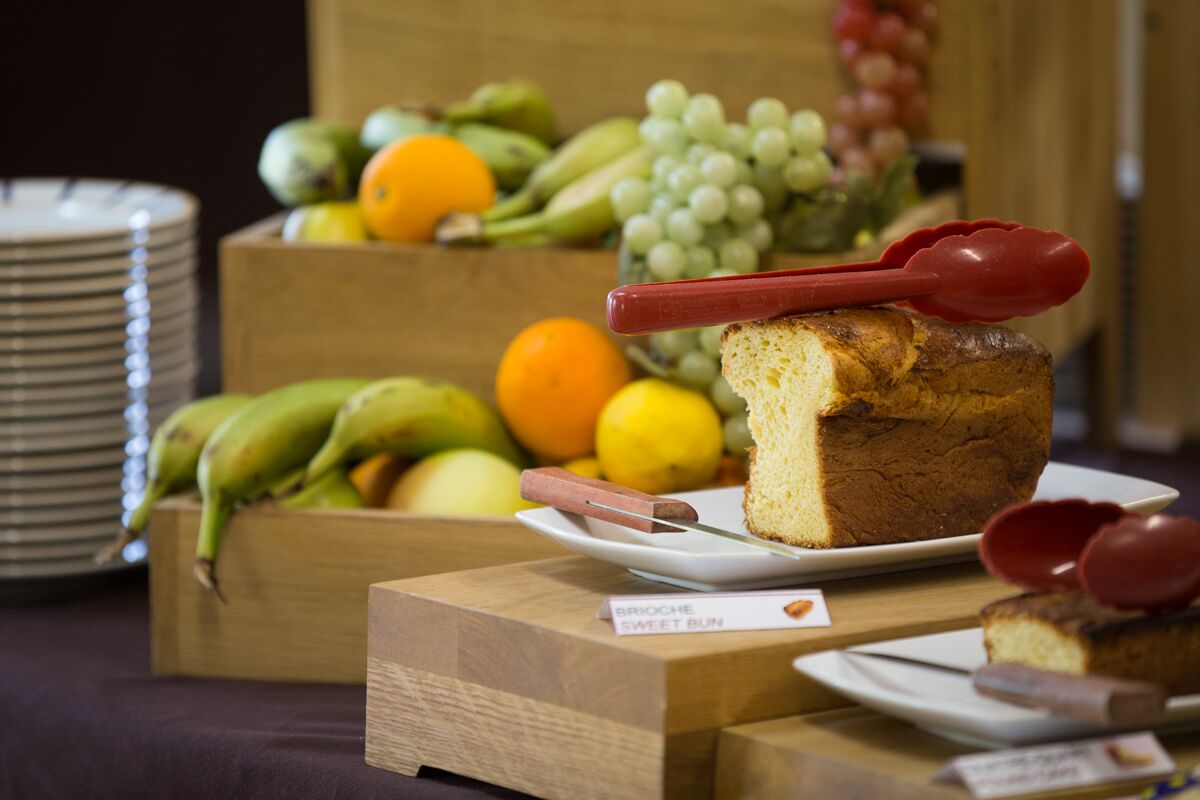 Uma mesa de madeira com um pão doce brioche, uma faca e uma colher vermelha sobre um prato branco.