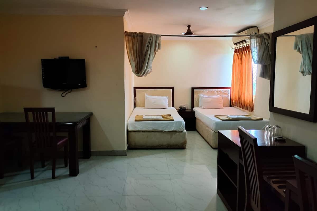 Quarto de hotel com duas camas de solteiro, uma escrivaninha com cadeira, televisão e espelho.
