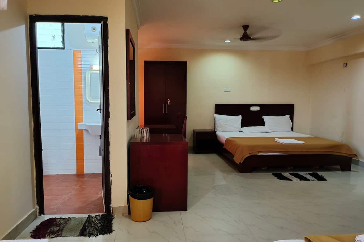 Quarto de hotel com cama, escrivaninha, lixeira e porta para um banheiro.