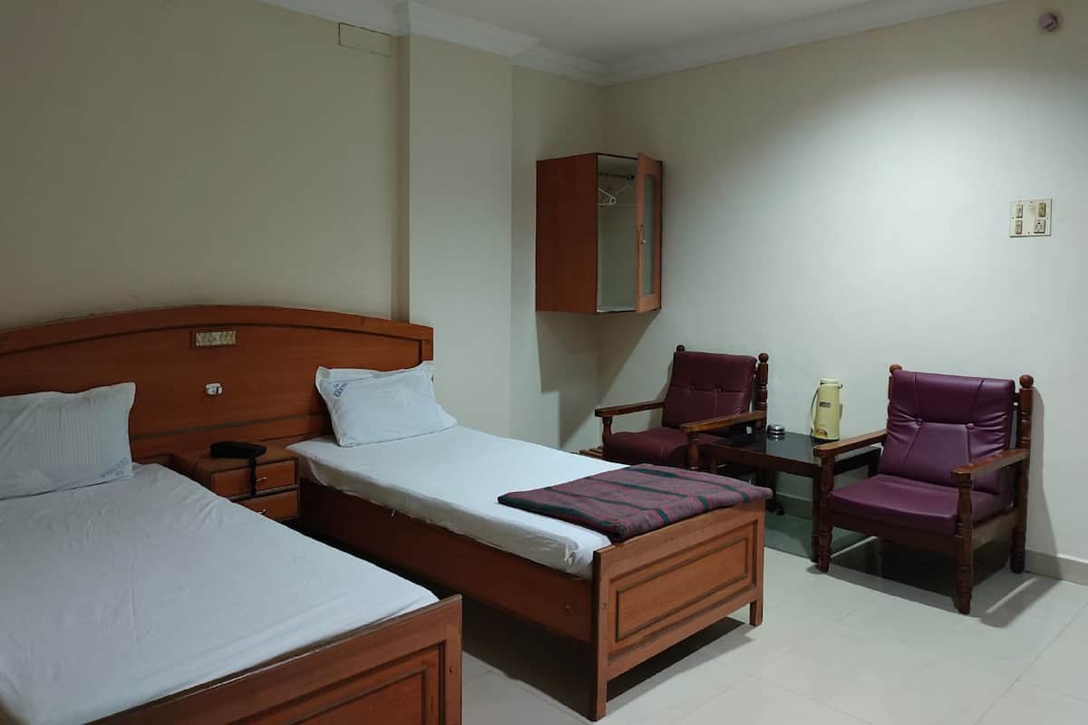 Quarto de hotel com duas camas de madeira, uma cadeira de madeira, uma mesinha e um armário.