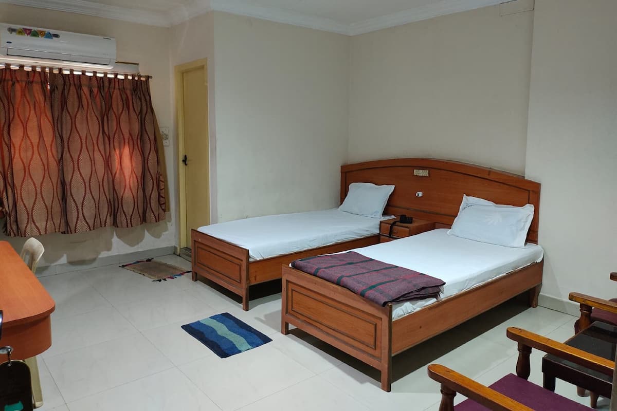 Quarto com duas camas de solteiro, escrivaninha de madeira, cadeira e uma mesinha.