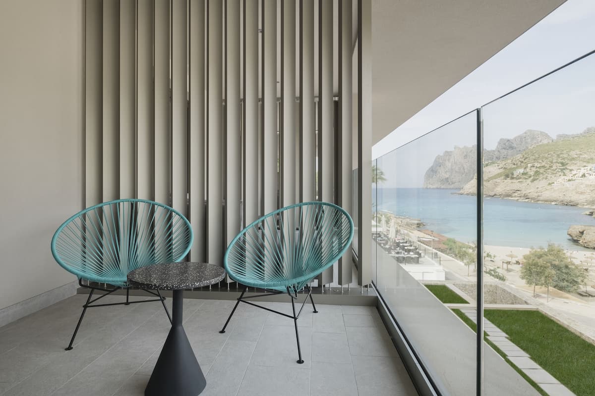 Varanda com duas cadeiras turquesa e uma pequena mesa, com vista para a paisagem costeira com terreno rochoso e uma visão clara do mar.