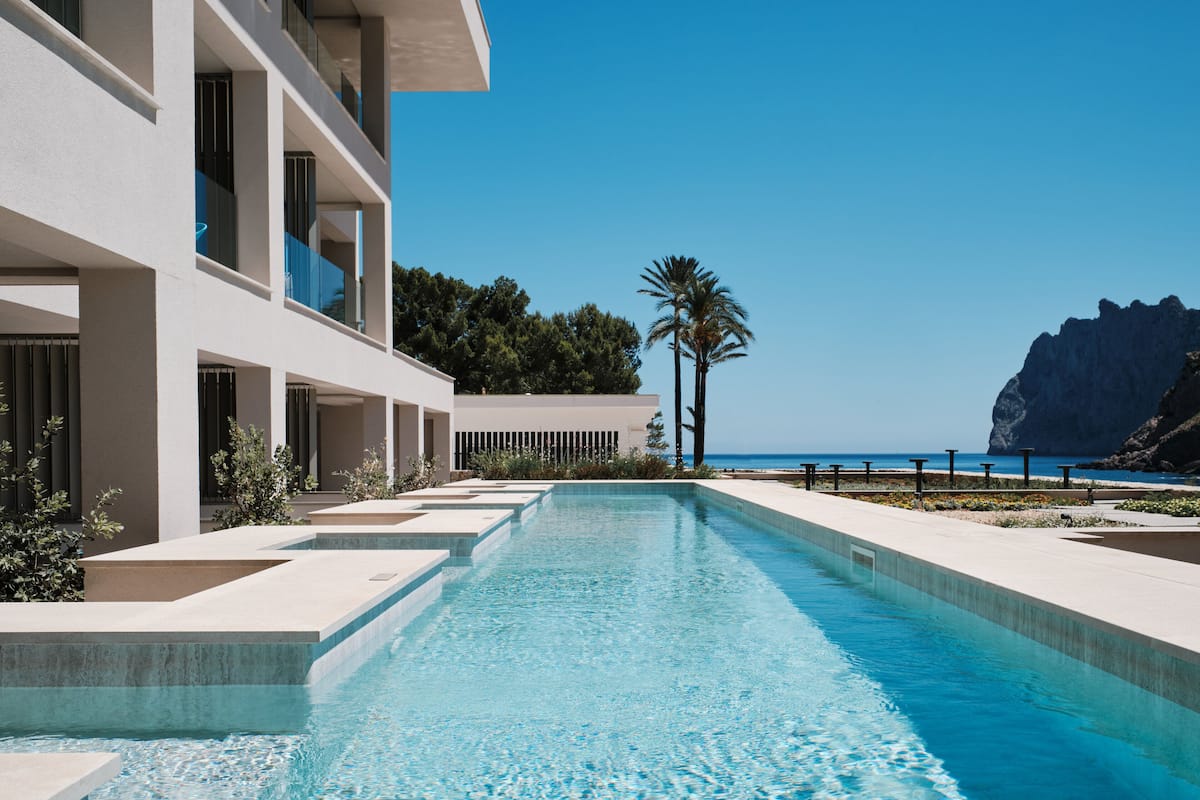 Um hotel moderno com piscina, vista para o mar e um penhasco rochoso.