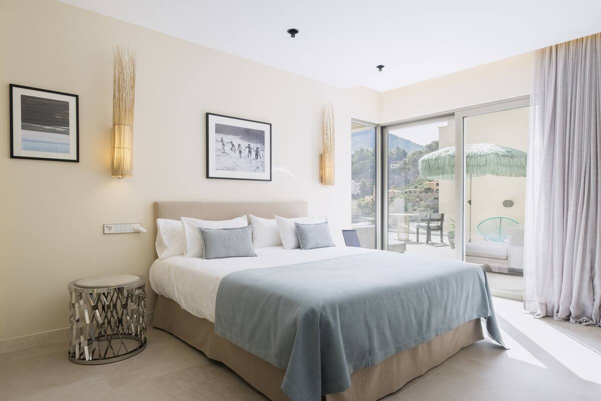 Quarto com cama, mesa de cabeceira e uma janela grande com vista para o exterior.
