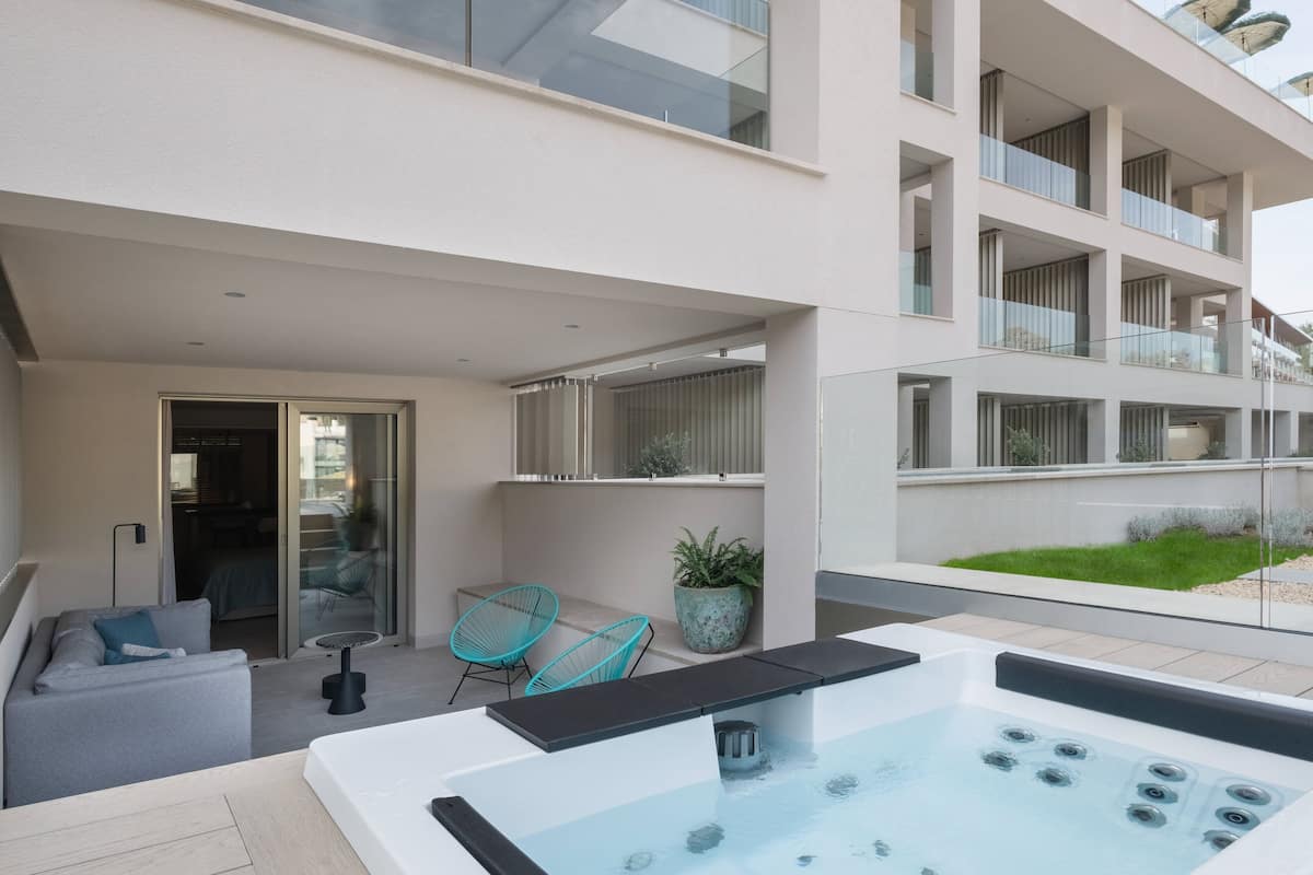 Uma área externa moderna com hidromassagem, assentos e guarda-corpo de vidro com vista para um jardim.