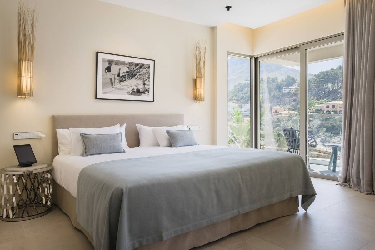 Quarto de hotel moderno com uma cama grande, vista para o campo e uma mesa lateral com um laptop.