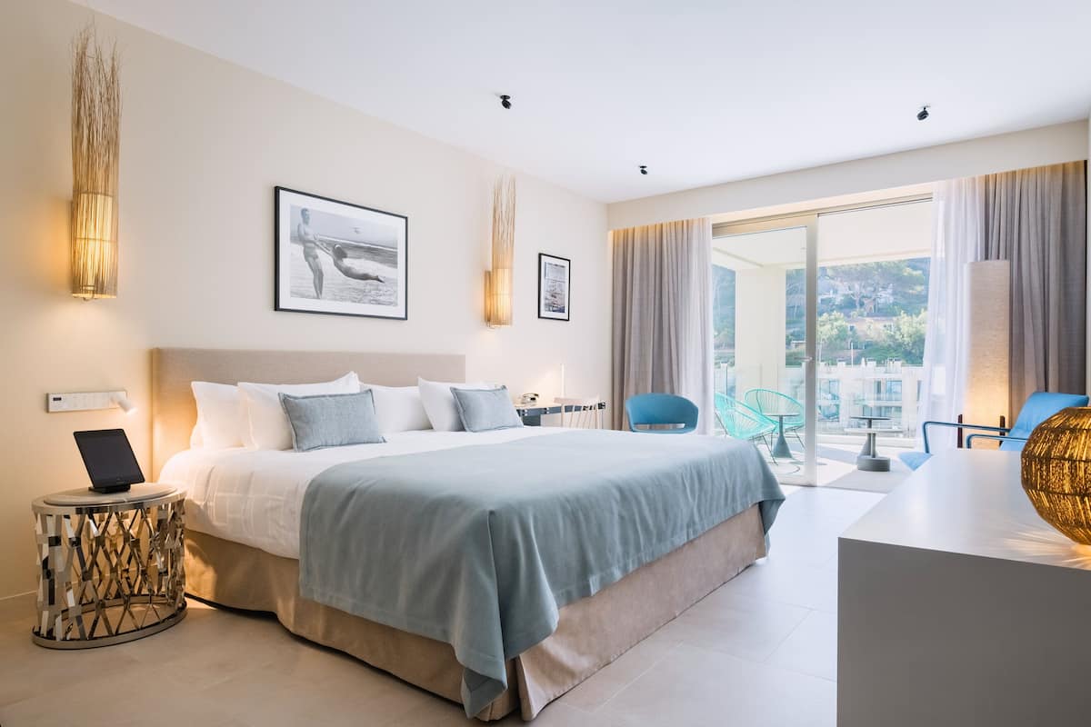 Quarto de hotel moderno com uma cama grande, mesas de cabeceira, uma escrivaninha e uma varanda com área de estar externa.